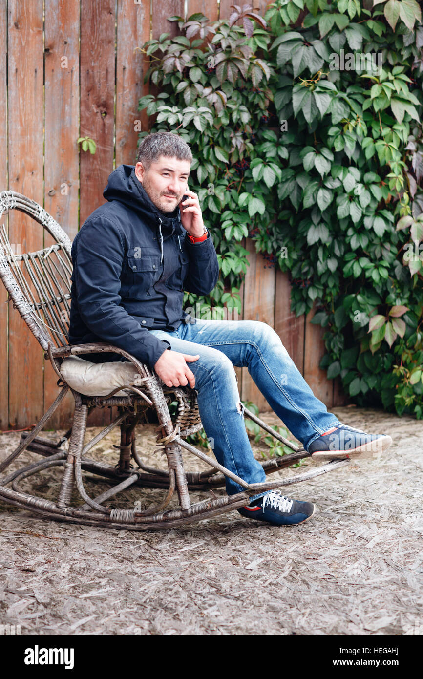 Handsome man relax in vintage rocking-chair with phone in garden Stock ...
