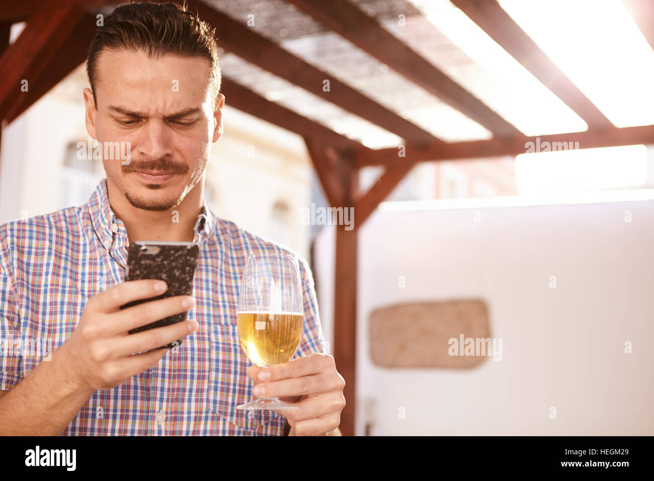 Good looking man frowning at his cellphone with a beer in one hand with ...