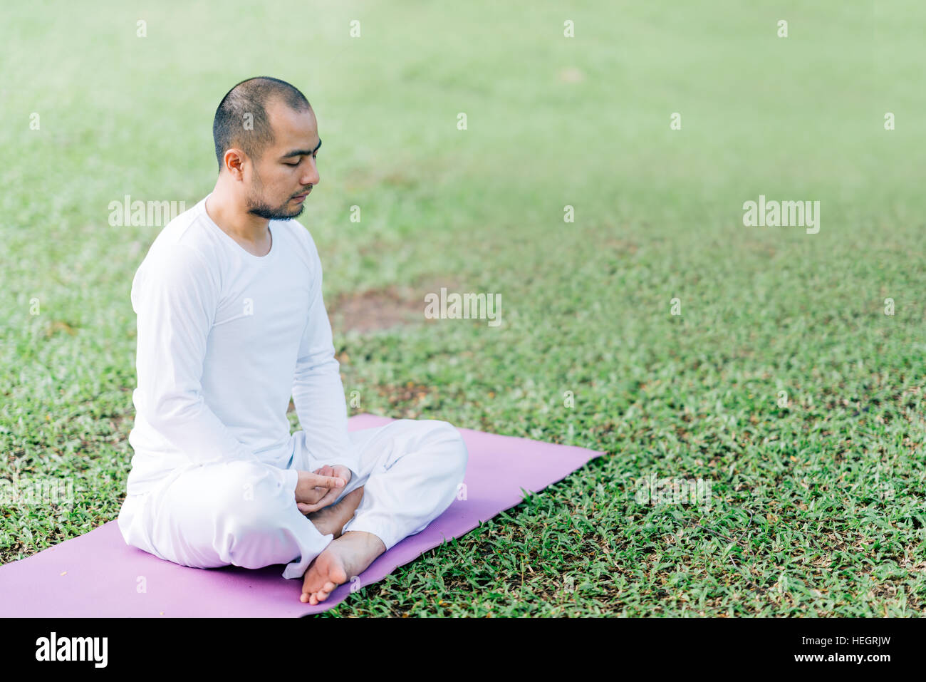 Handsome Asian man meditating on green grass in the park, calm and ...