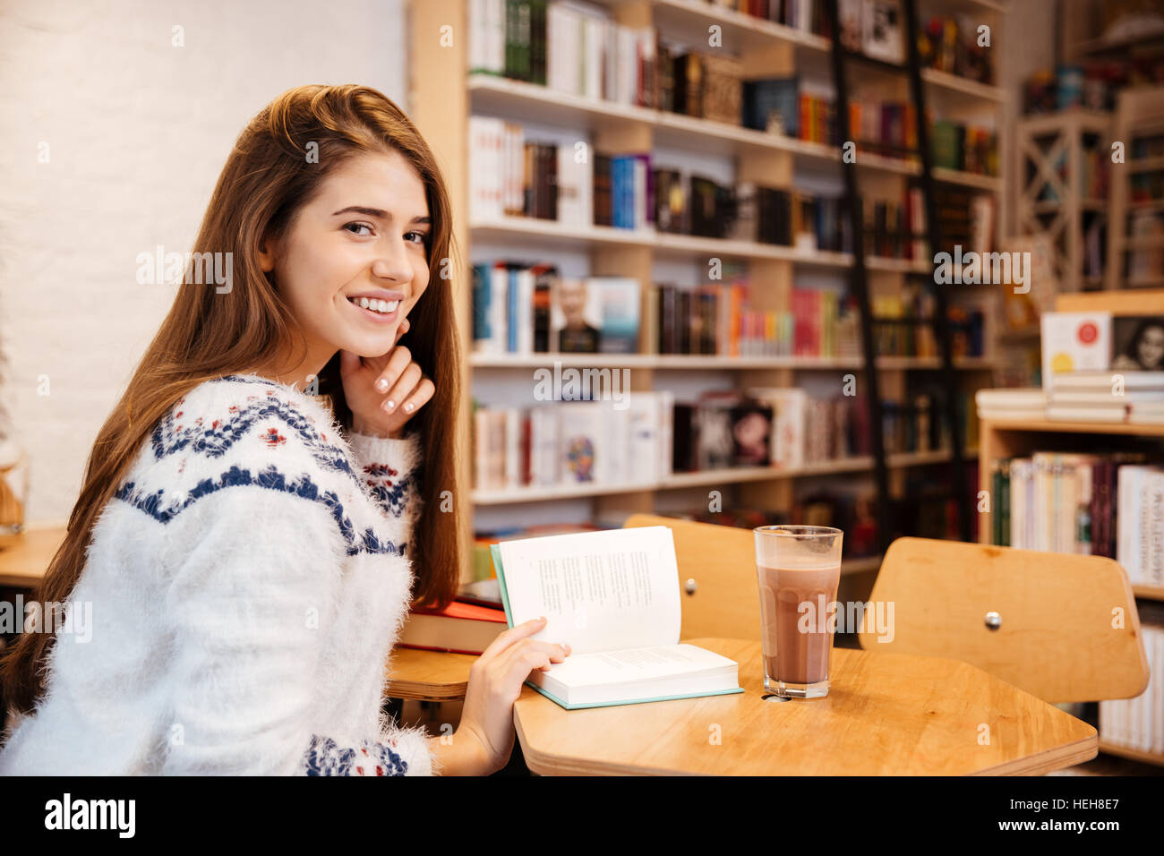 Happy smiling girl sitting at the table and reading book in library ...