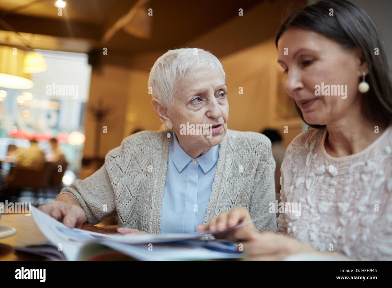 Senior woman talking to her friend while both looking through magazine ...