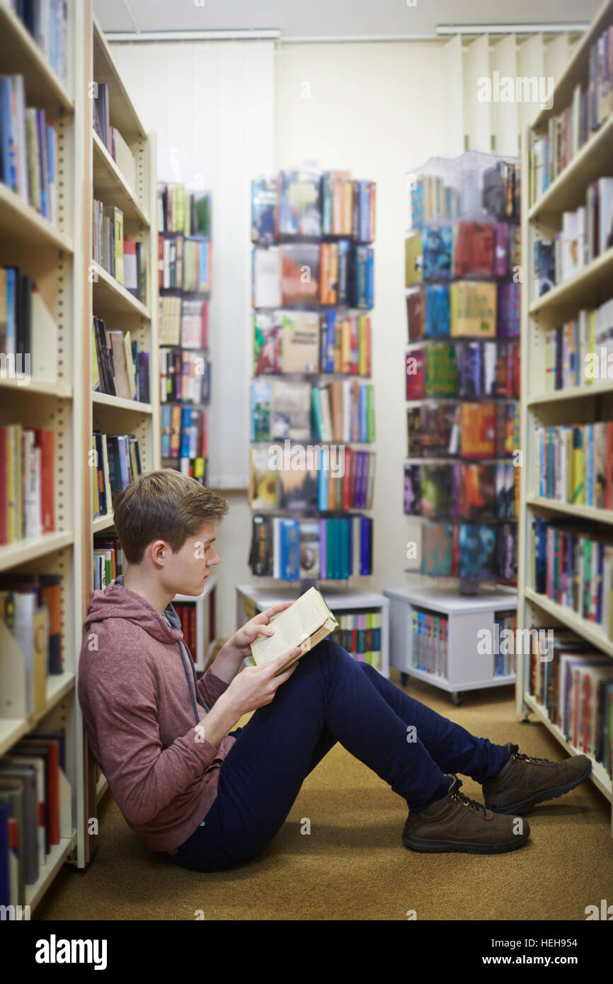 Serious guy sitting in library aisle with open book at leisure Stock ...
