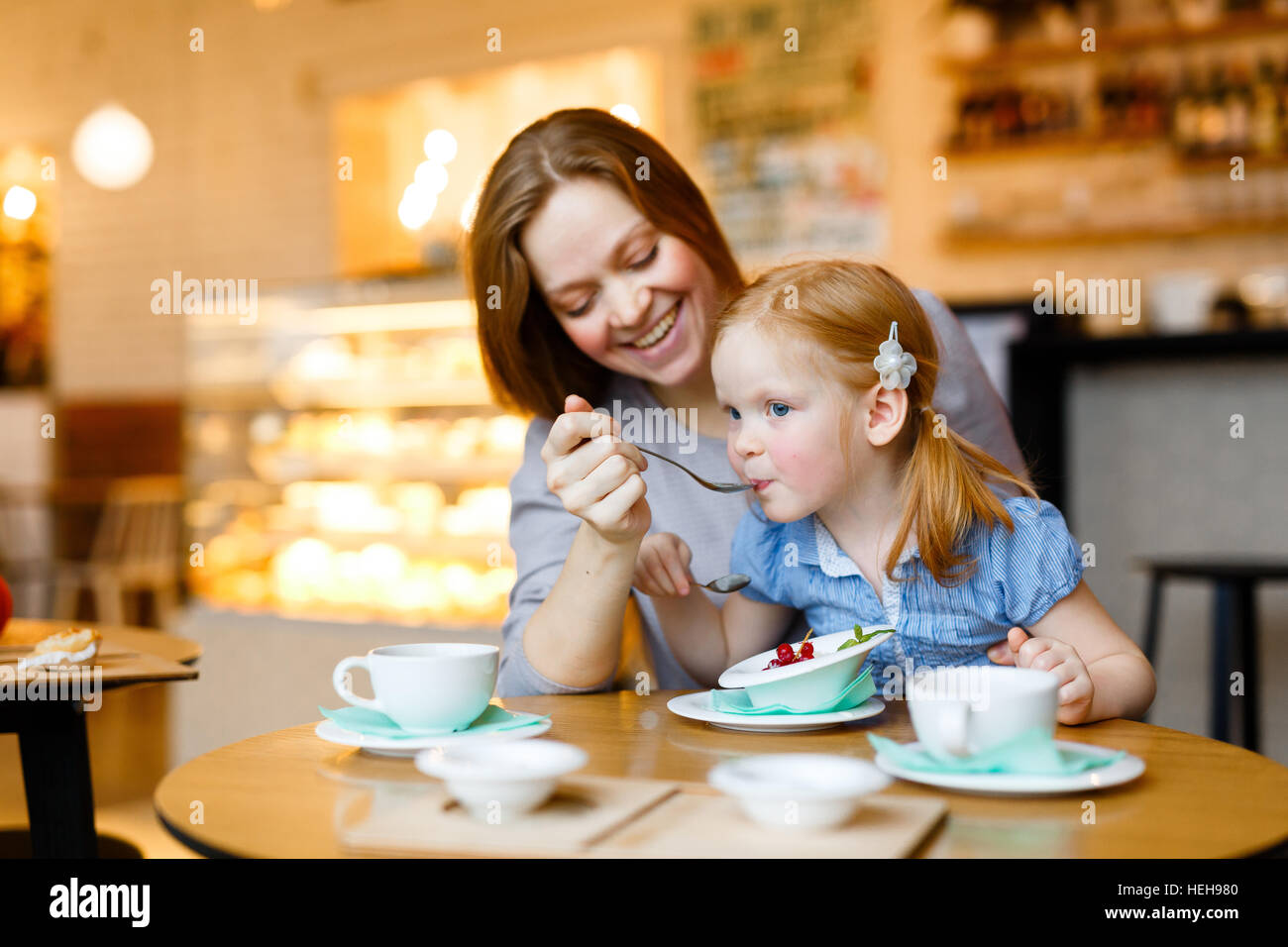 Little girl tasting dessert from spoon in cafe with mother near by ...
