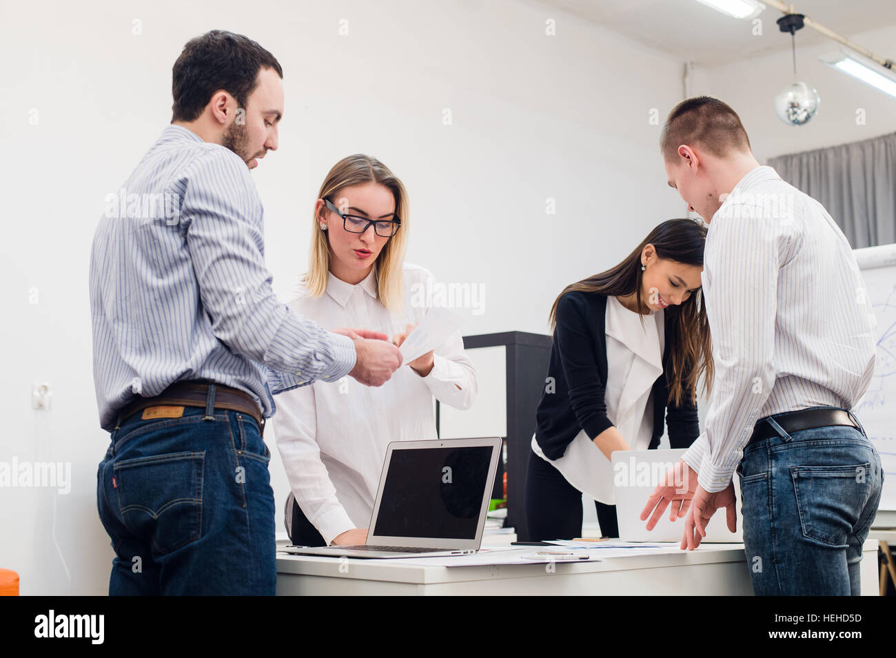 Four young business people working as a team gathered around laptop ...