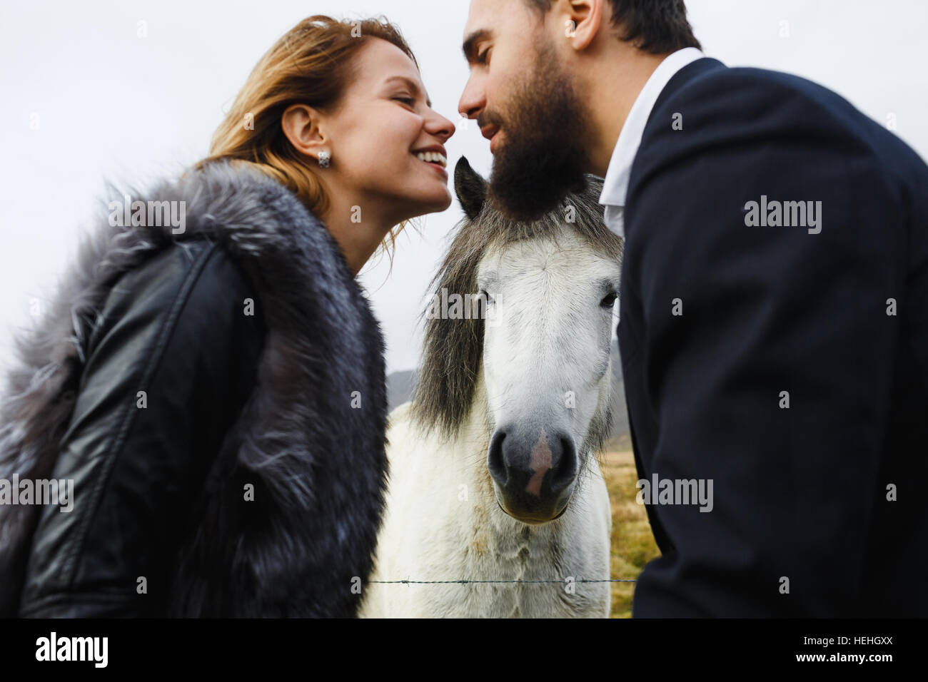 Amorous man and woman looking at one another with horse between them ...