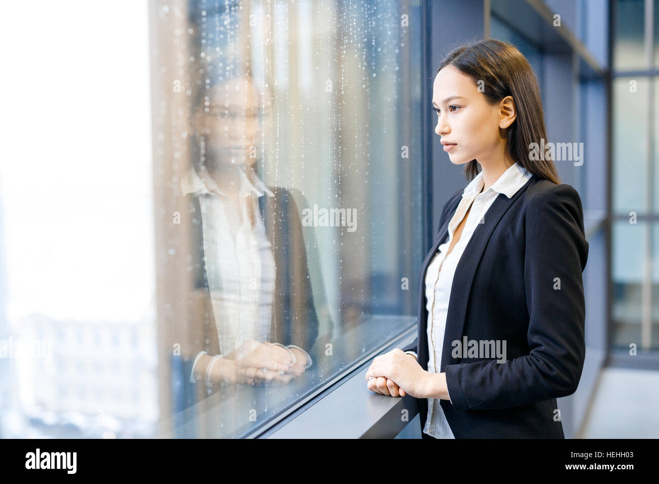 Businesswoman in formalwear looking through office window on rainy day ...