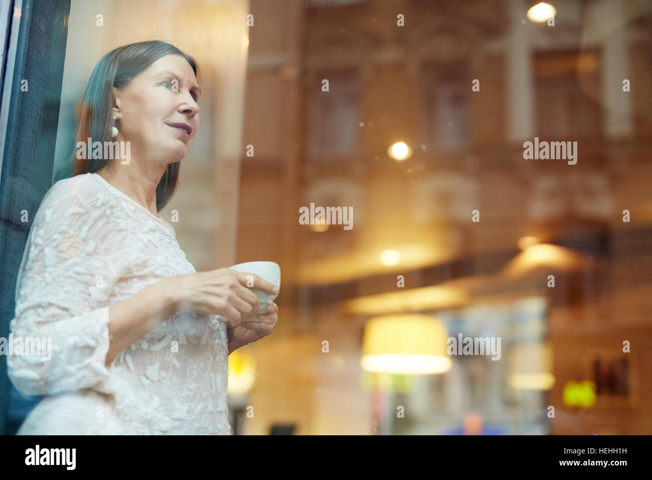 Restful female with cup of tea looking through cafe window Stock Photo ...