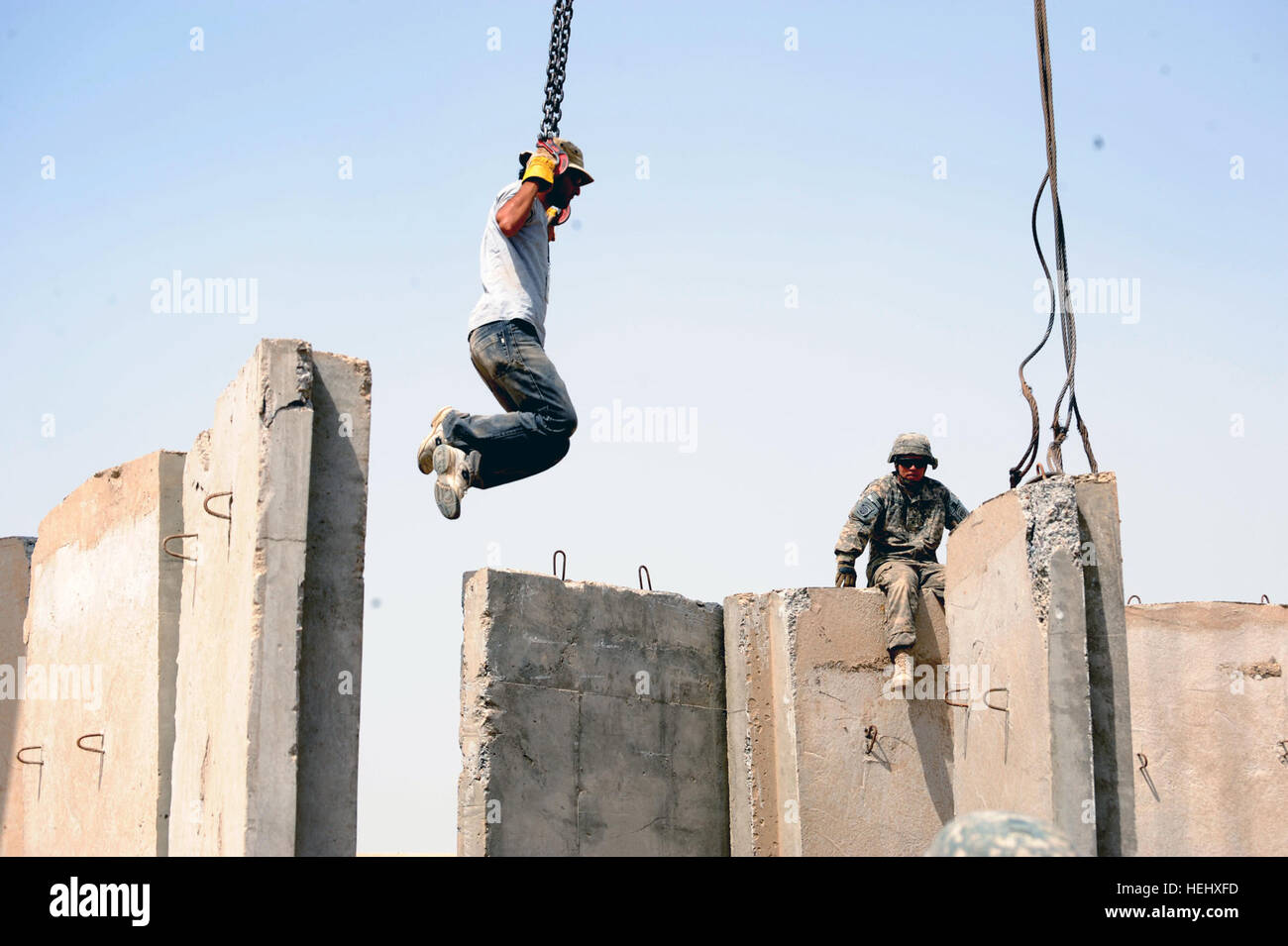 An Iraqi worker holds onto chains suspended from a crane as U.S. Army ...