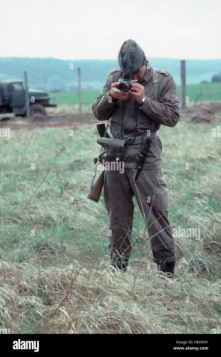 An armed East German soldier takes a photograph along the border ...