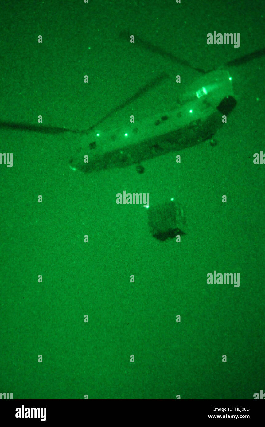 A U.S. Army CH-47 Chinook helicopter carries a sling-loaded container and hovers above the ...