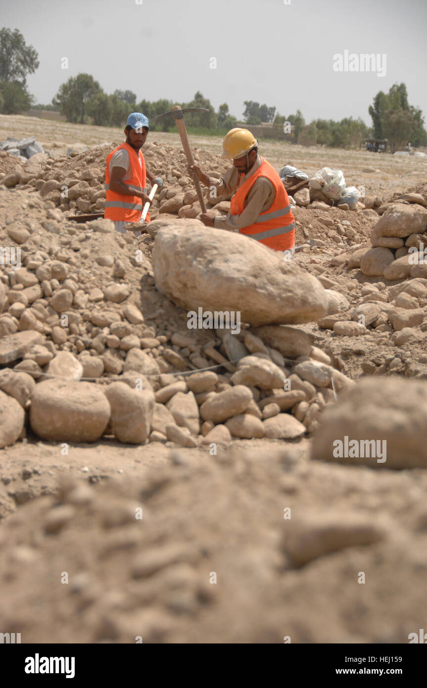 Construction workers chip and dig away at rocks in the rough terrain ...