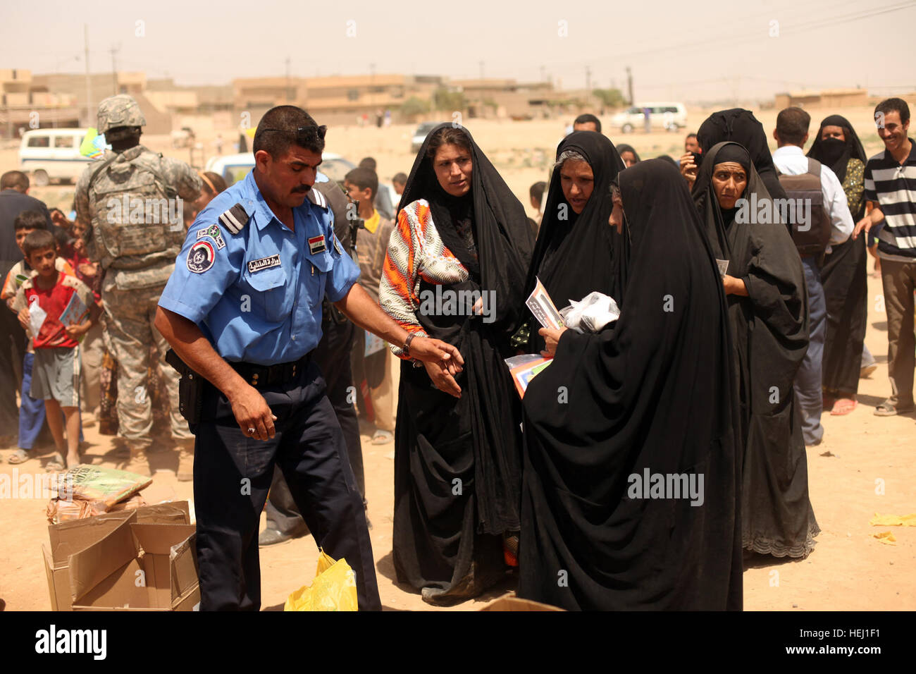 An Iraqi police officer hands bags of supplies to Iraqi women during a ...