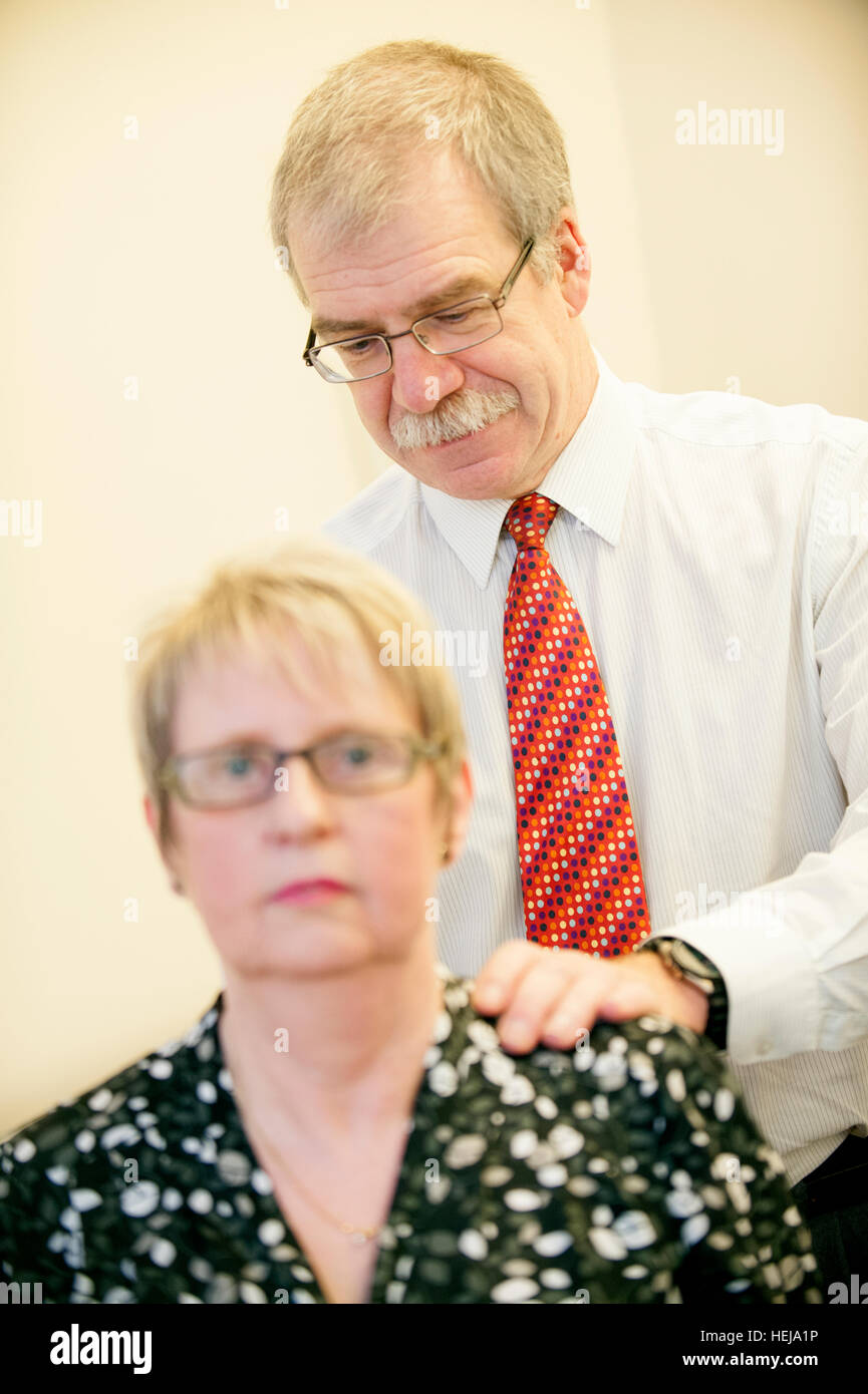 White male GP rests hand on patients back, during a back examination in ...