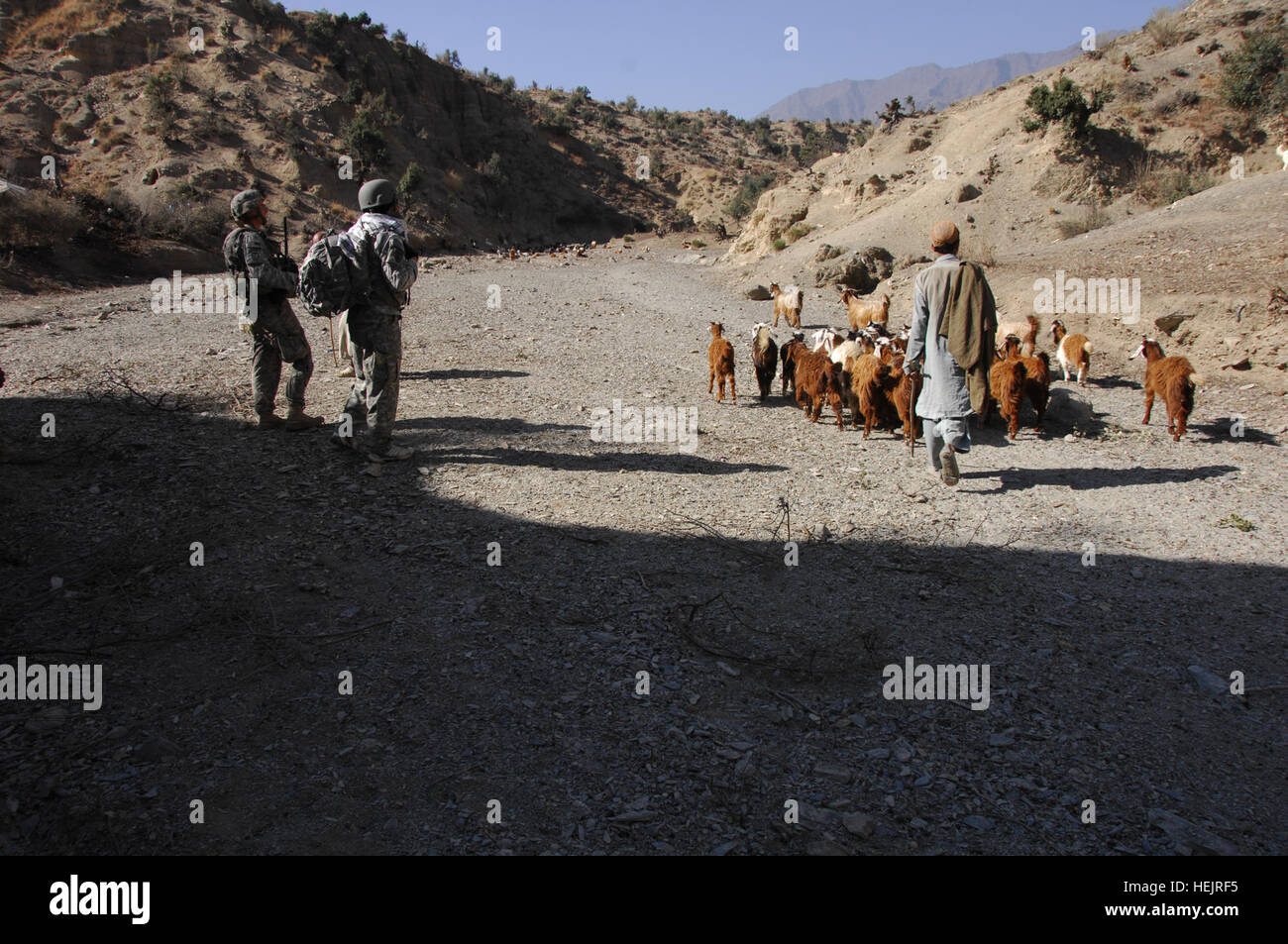 Two U.S. Army Soldiers watch as a young Afghan boy herds his goats ...