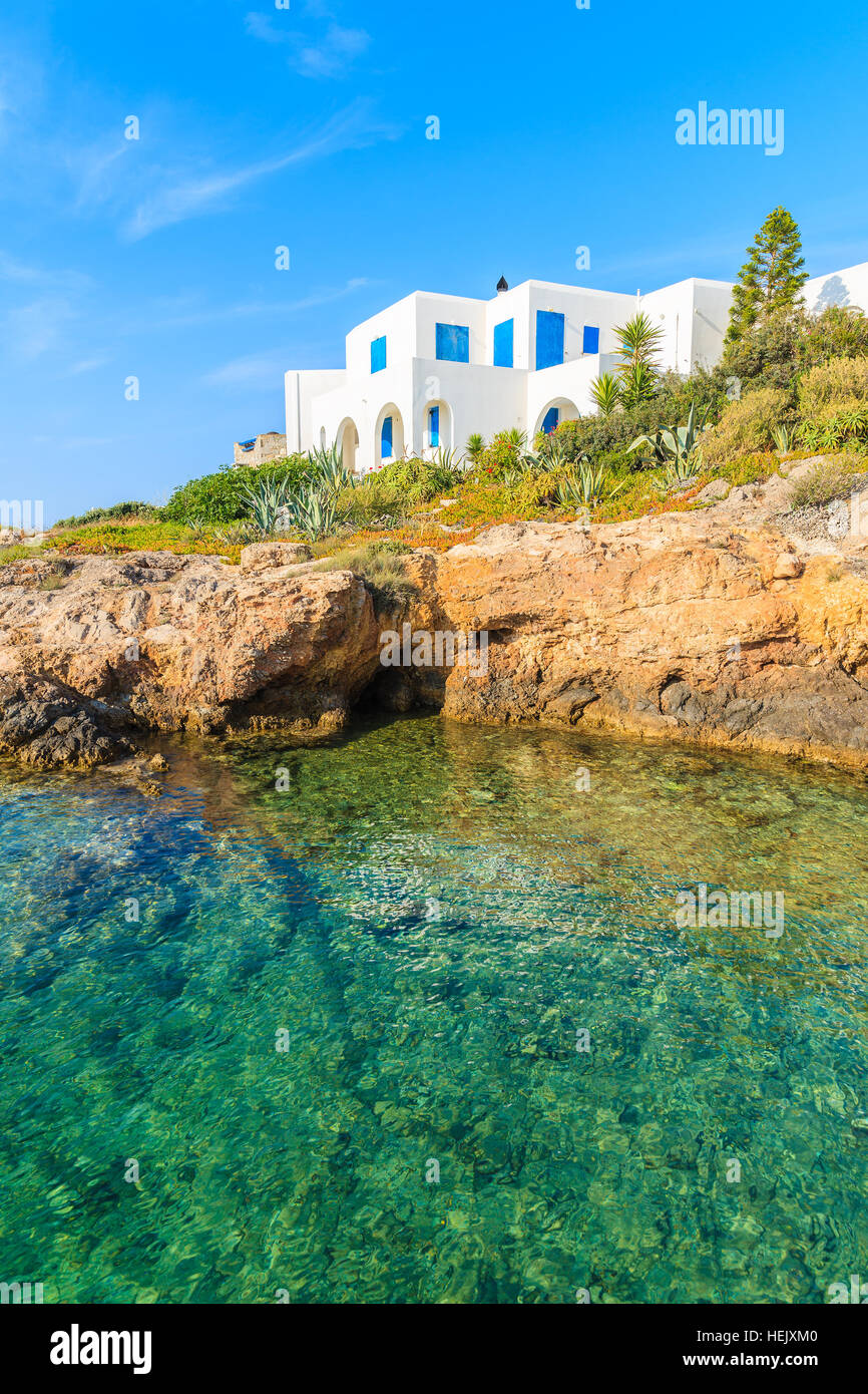 White typical Greek house on cliff overlooking beautiful sea cove with ...