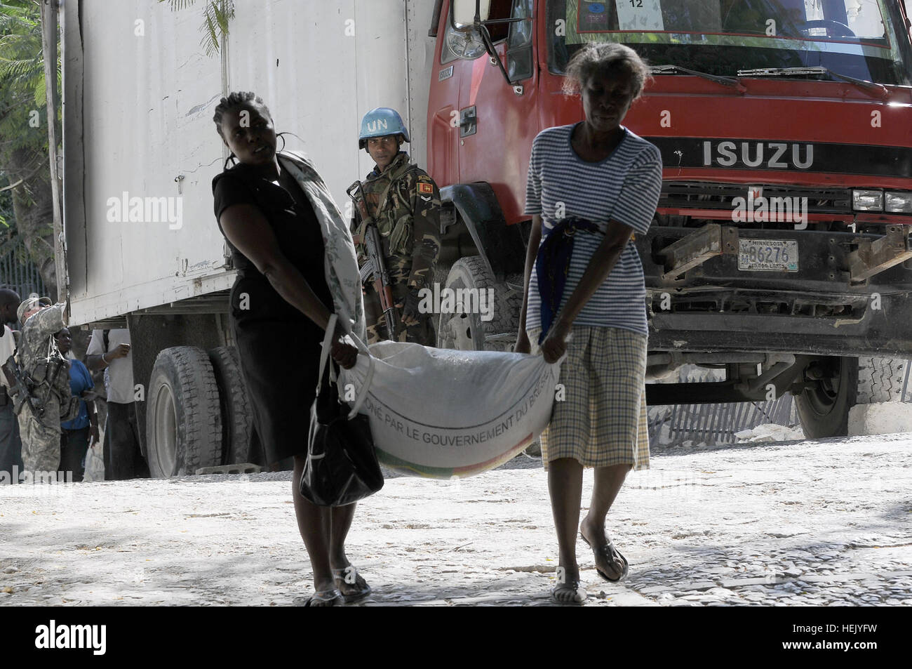 A two Haitian women struggle to carry a 50Kg bag of rice they received ...