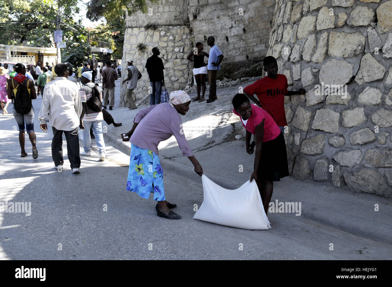 A two Haitian woman struggle to drag a 50Kg bag of rice they received ...