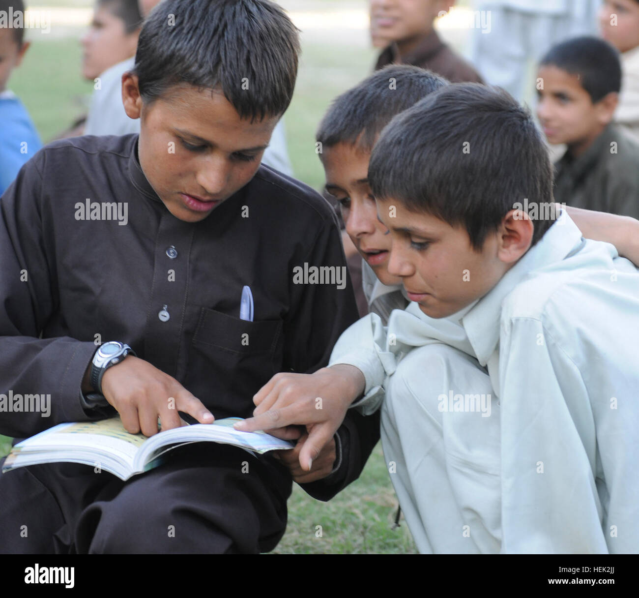 A group of Afghan youth look through a copy of the Boy Scout handbook ...