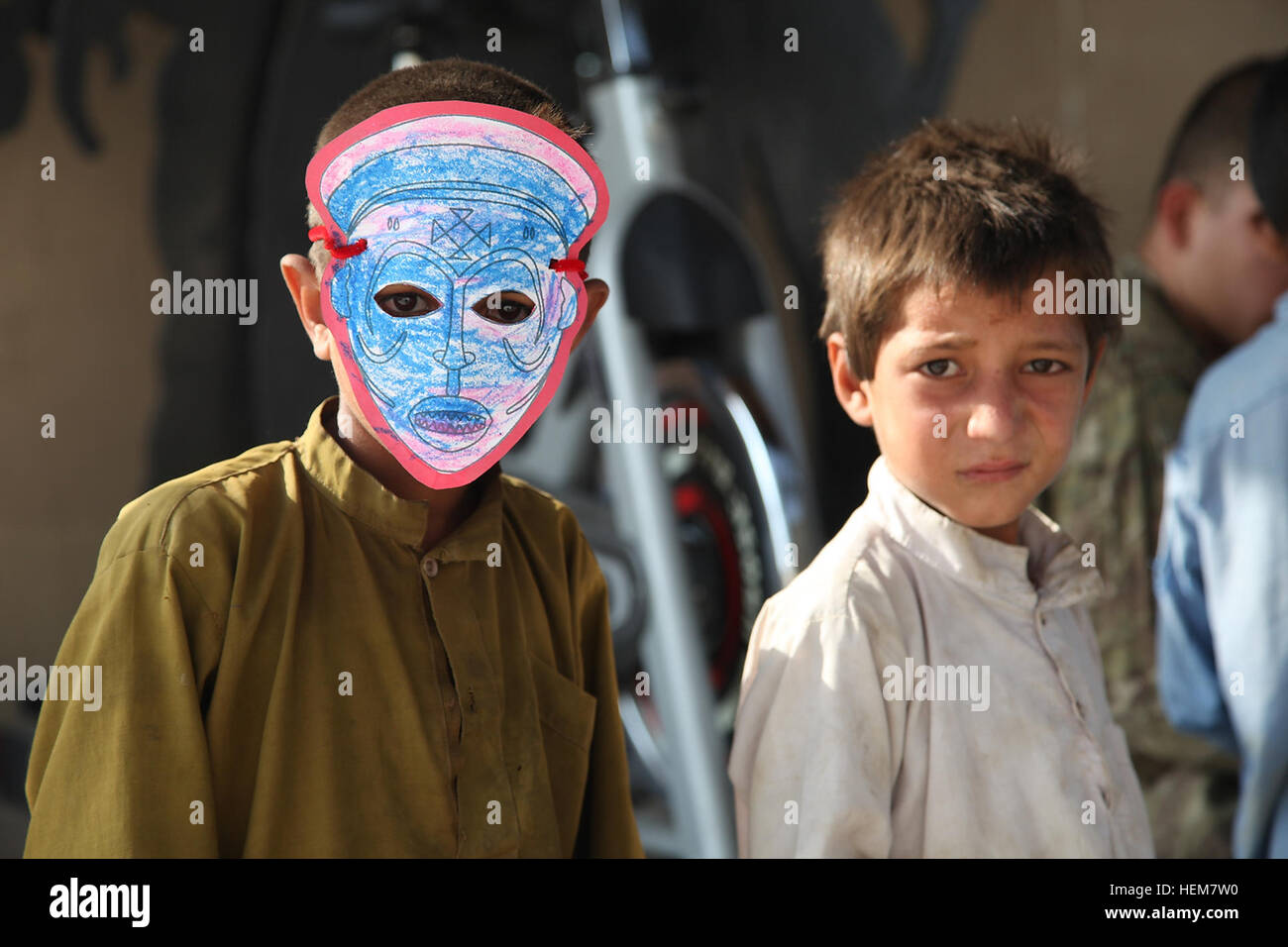 An Afghan boy shows the mask he made while his counterpart looks into ...