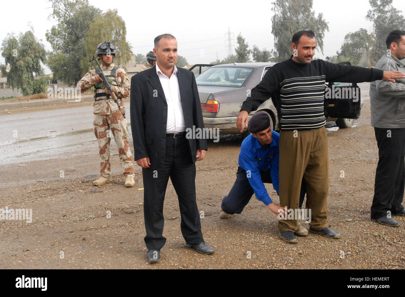 An Iraqi policeman searches Iraqi civilians as his Iraqi army ...