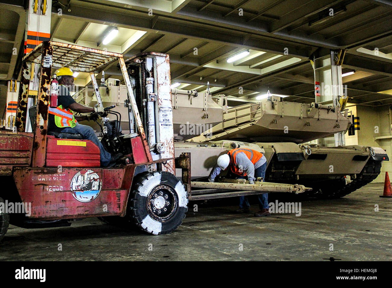 Contractors work to attach a tow bar onto an Abrams tank to pull out of ...