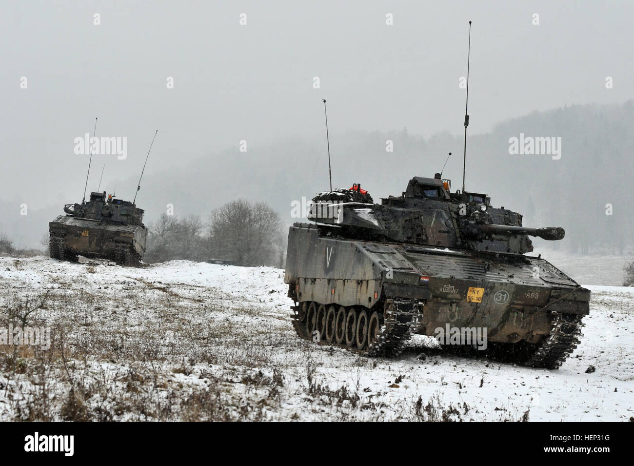 Two Dutch CV 90 combat vehicles maneuver through snow covered terrain ...