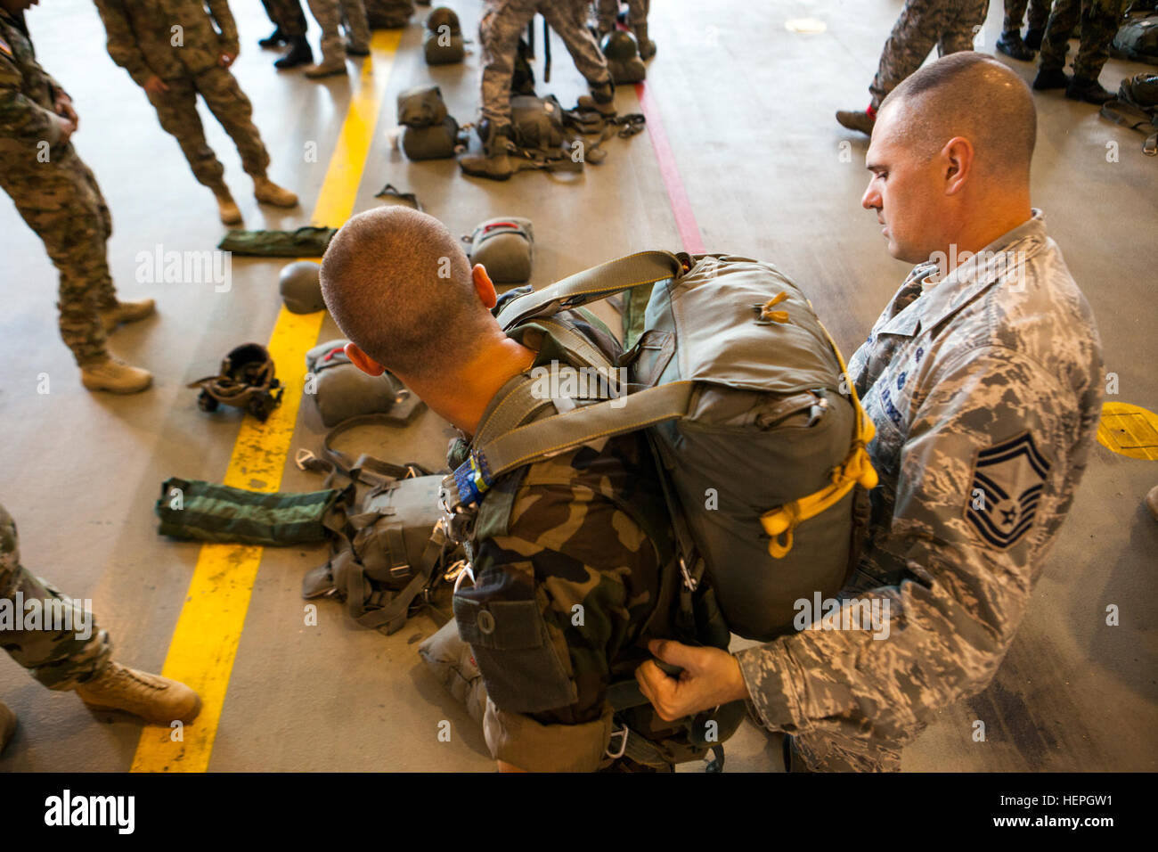 A U.S. Air Force paratrooper assists a French paratrooper with putting ...