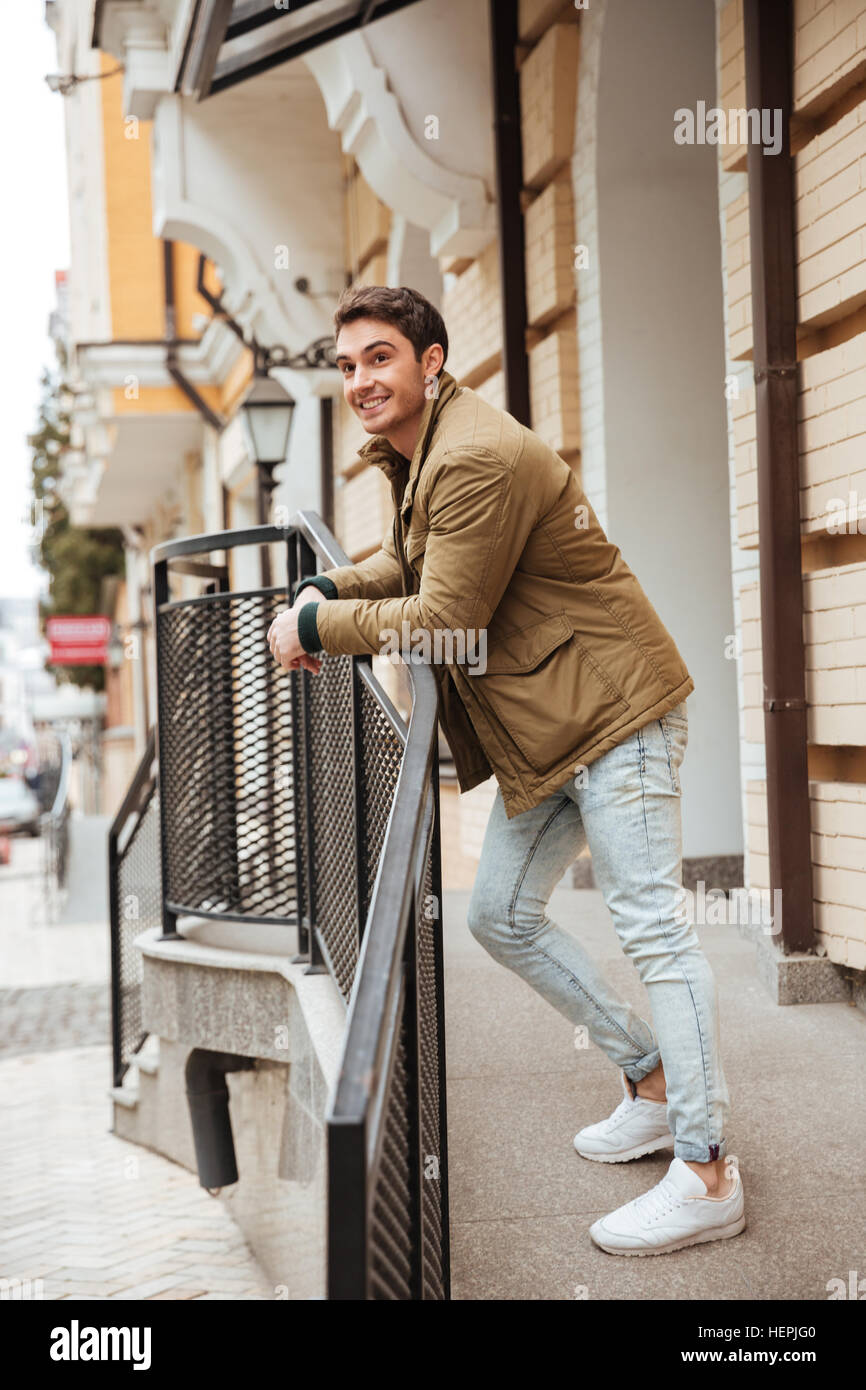 Image of cheerful young man walking on the street and looking aside ...