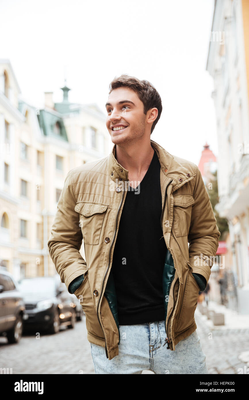 Photo of cheerful young man walking on the street and looking aside ...