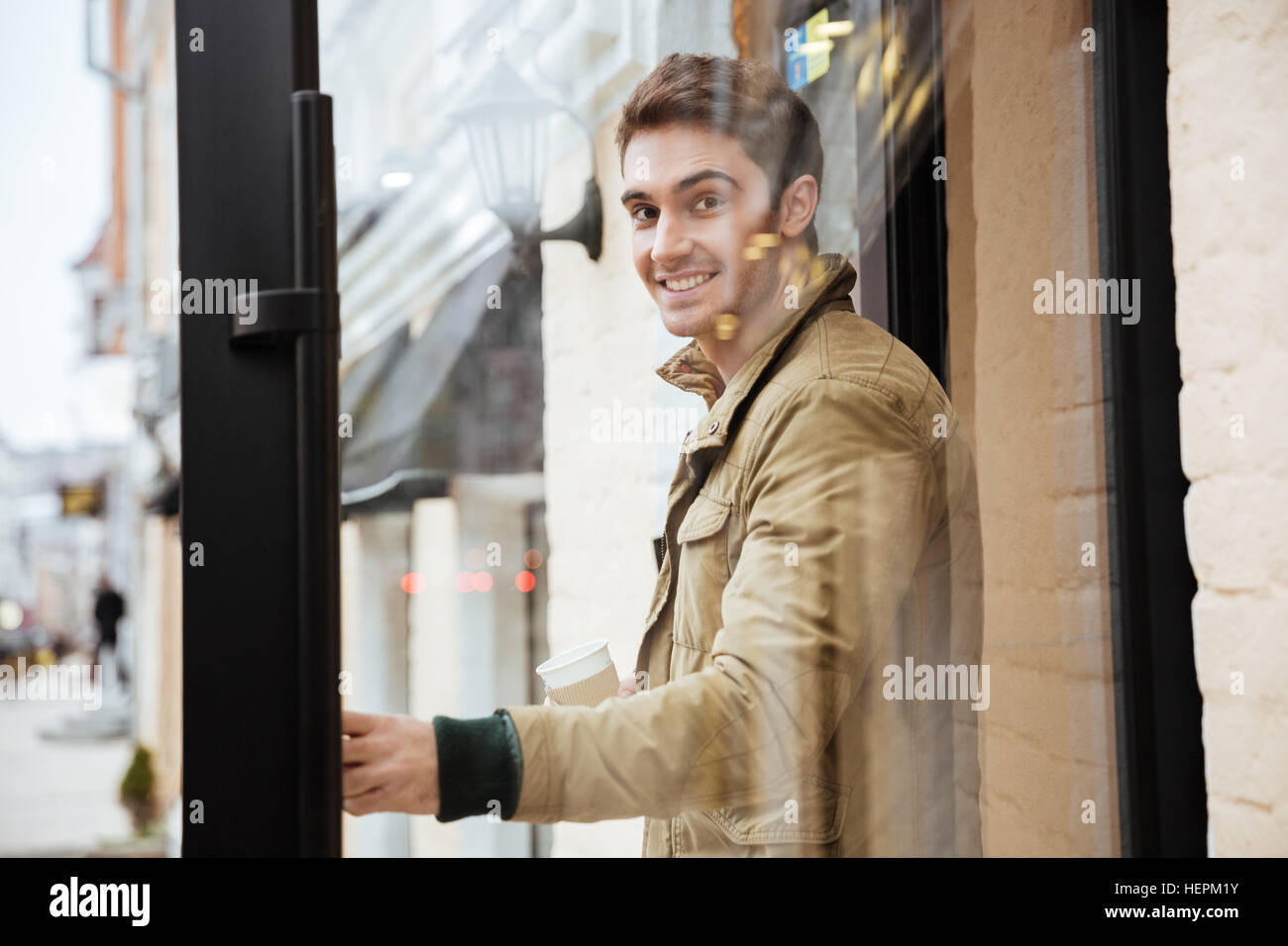 Picture of cheerful young man walking on the street and looking at ...