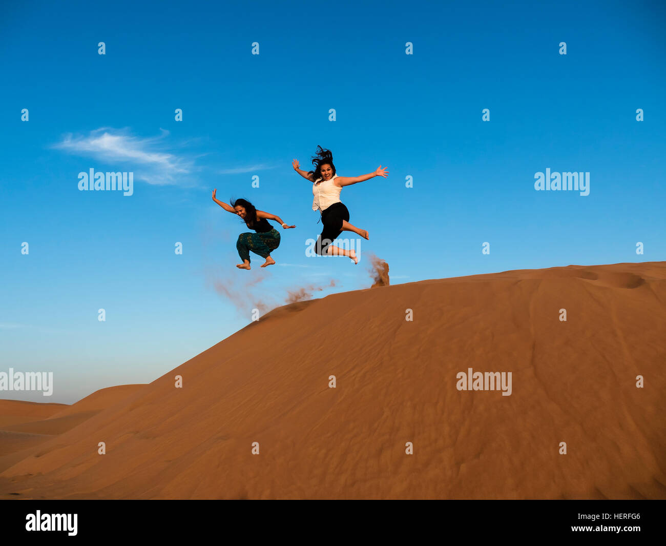 Two young women jumping from sand dune in desert, Sharqiya Sands or ...