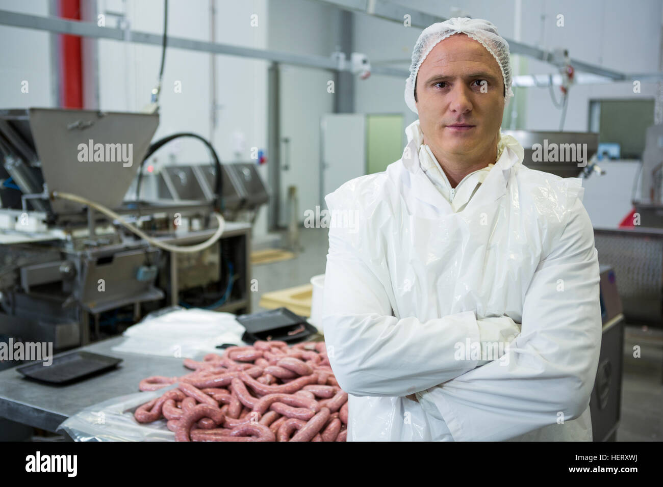 Portrait of male butcher standing with arms crossed at meat factory ...