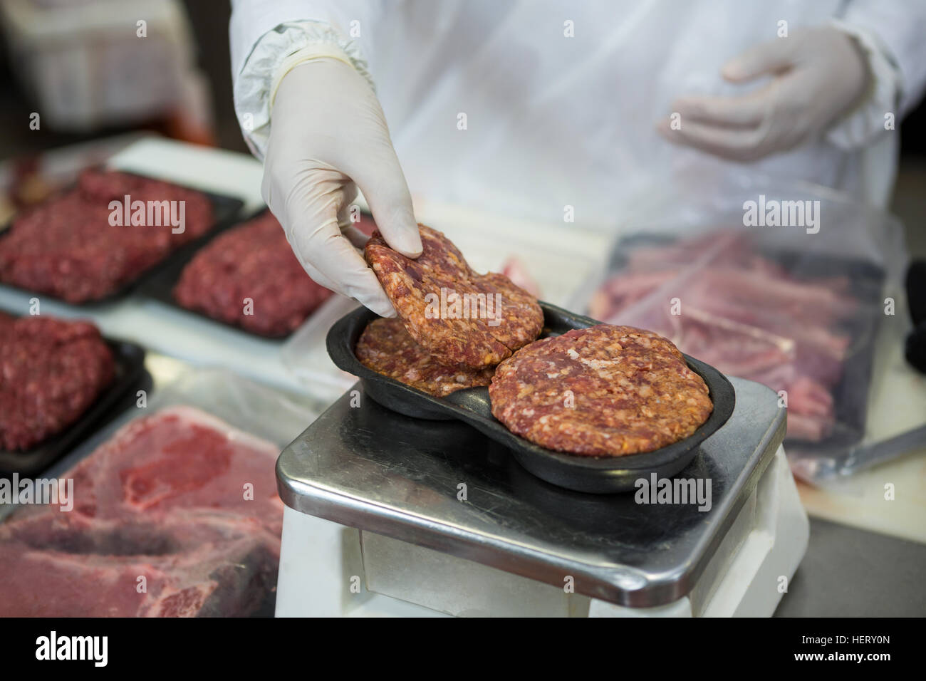 Close-up of butcher weighing meat patties on scale at meat factory ...