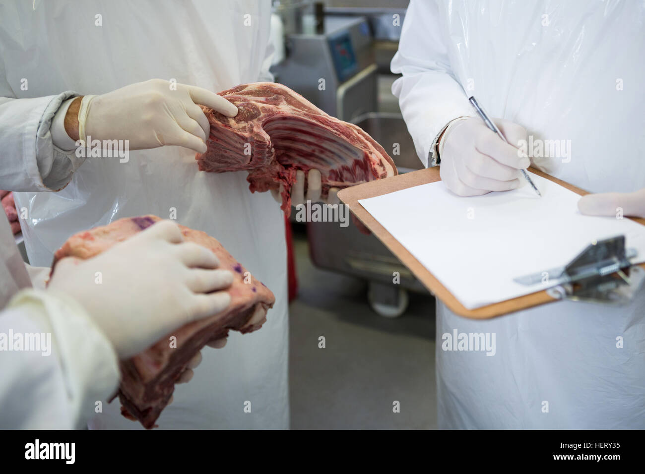 Mid section of butchers maintaining records on clipboard at meat ...