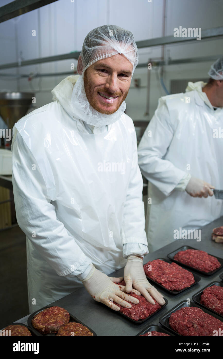 Portrait of smiling butcher arranging minced meat in packaging tray in ...