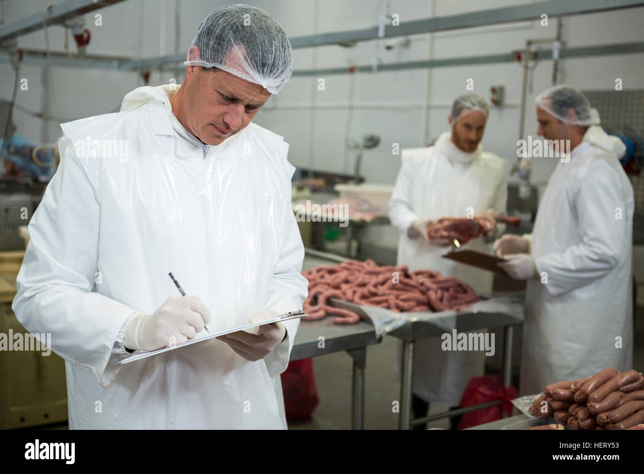 Male butcher maintaining records on clipboard at meat factory Stock ...