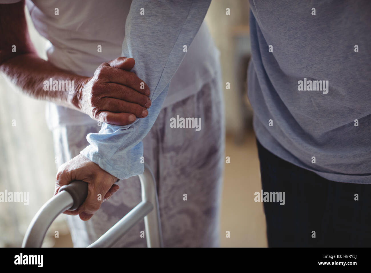 Senior woman helping senior man to walk with walker at home Stock Photo ...