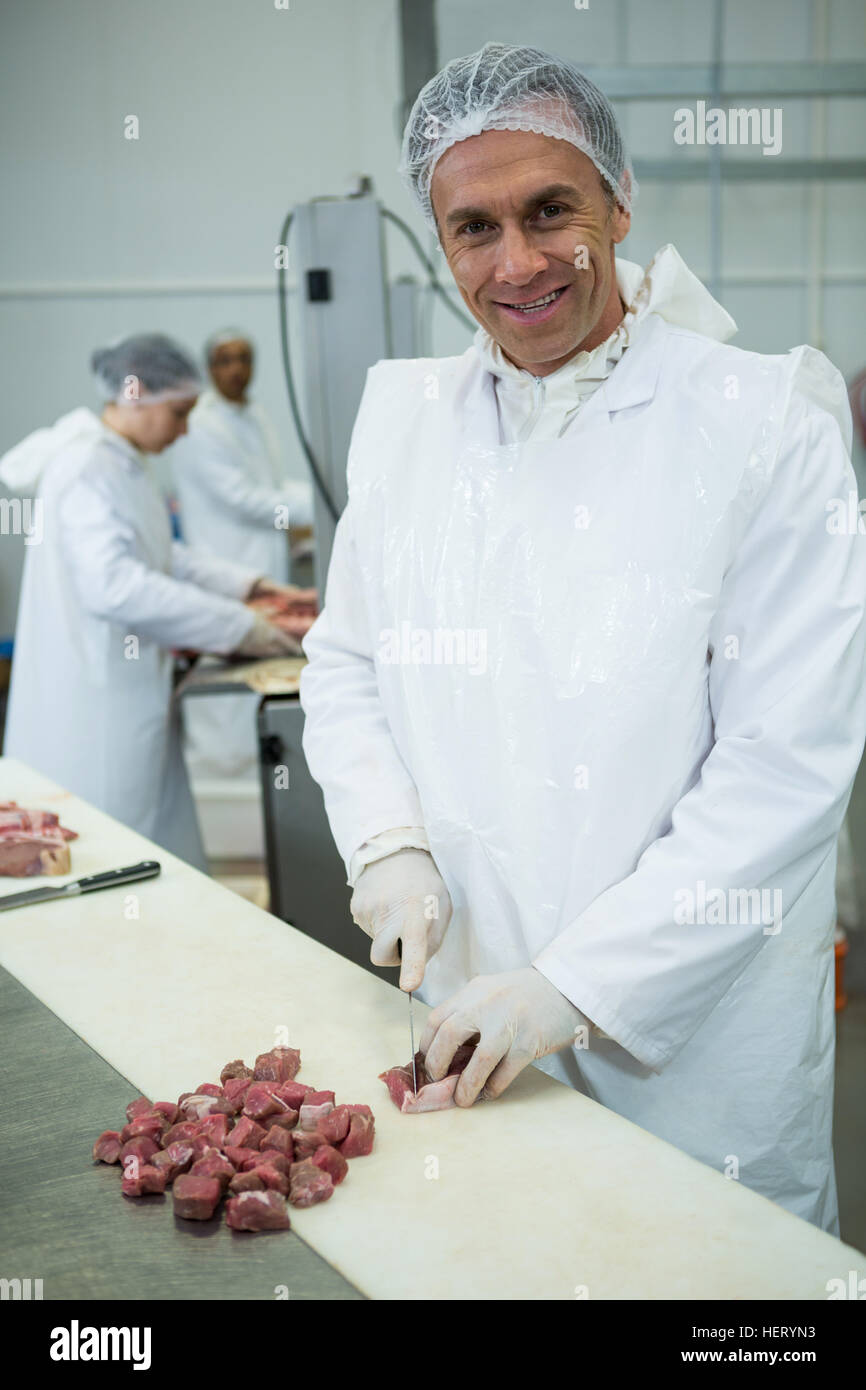Portrait of butcher cutting meat into small pieces at meat factory ...