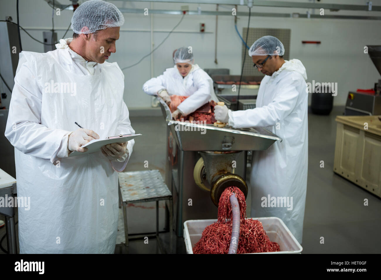 Butchers placing meat in mincing machine at meat factory Stock Photo ...