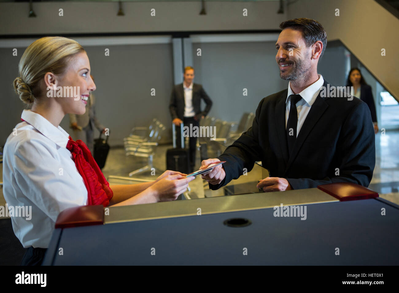 Female staff giving boarding pass to the businessman at the check in ...