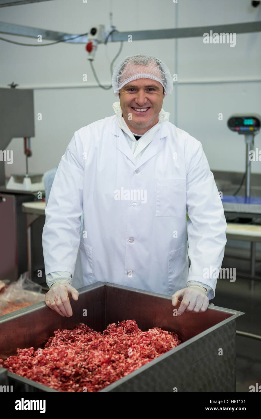Portrait of butcher standing with container full of minced meat in meat ...