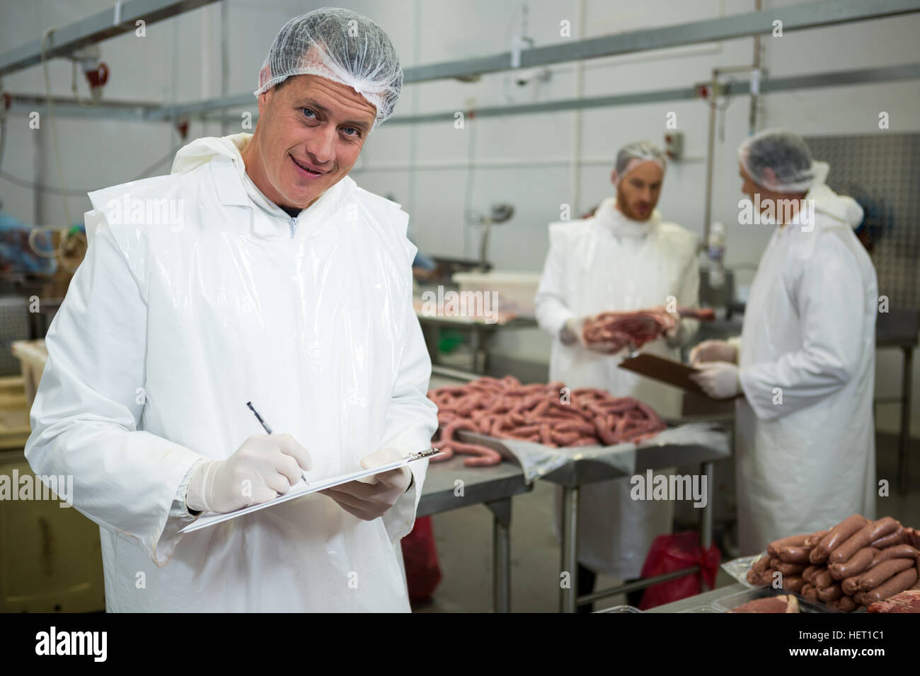 Portrait of male butcher maintaining records on clipboard at meat ...