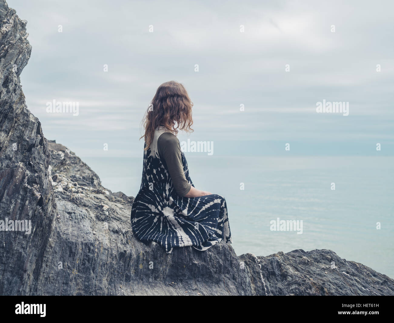 A young woman is sitting on some rocks by the sea Stock Photo - Alamy