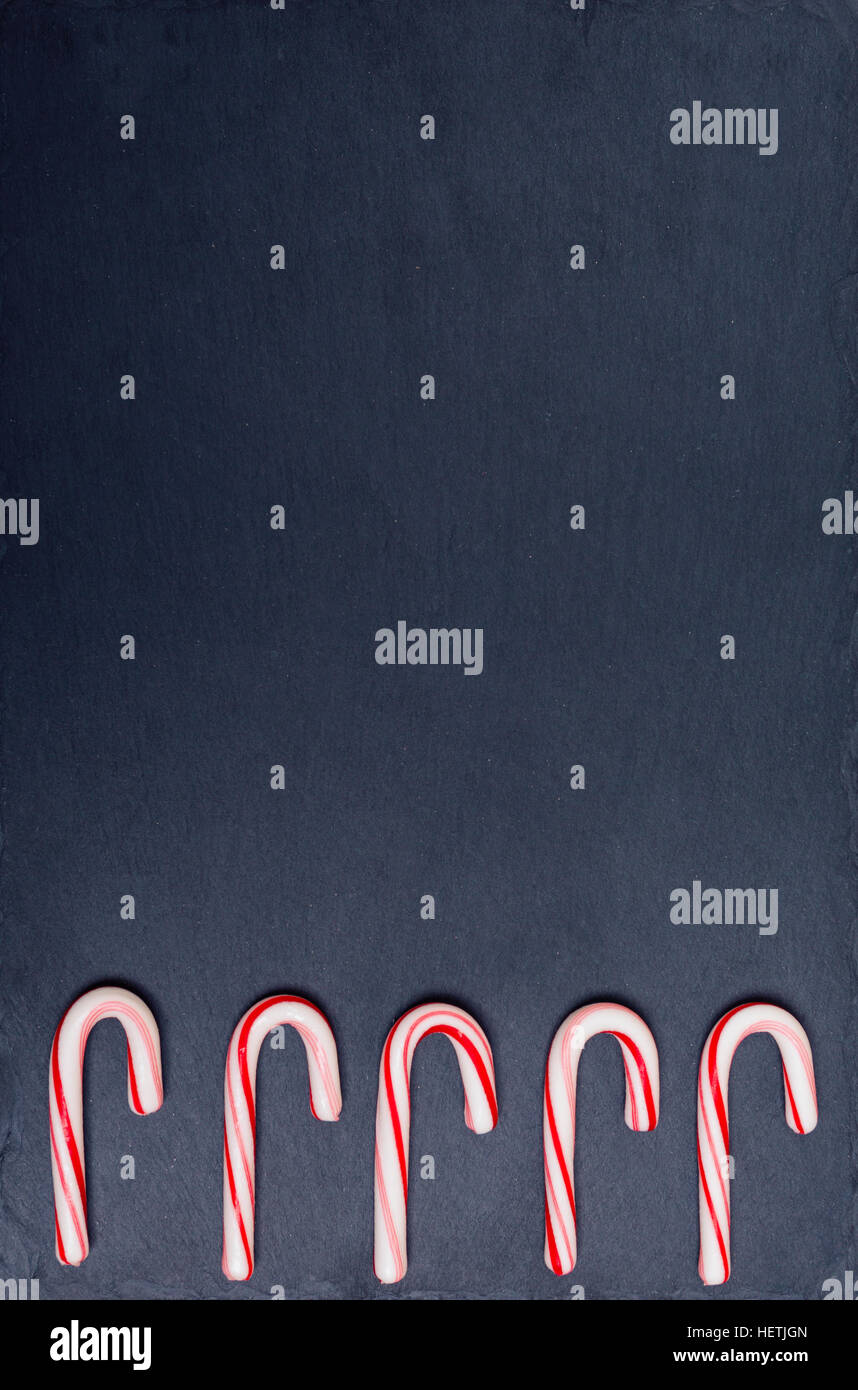 Five holiday striped candy canes in a row on dark stone background. Top ...