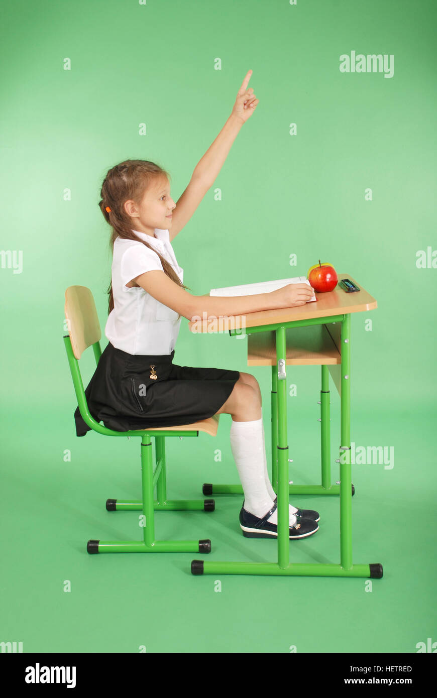 Girl in a school uniform raising hand to ask question isolated on green ...
