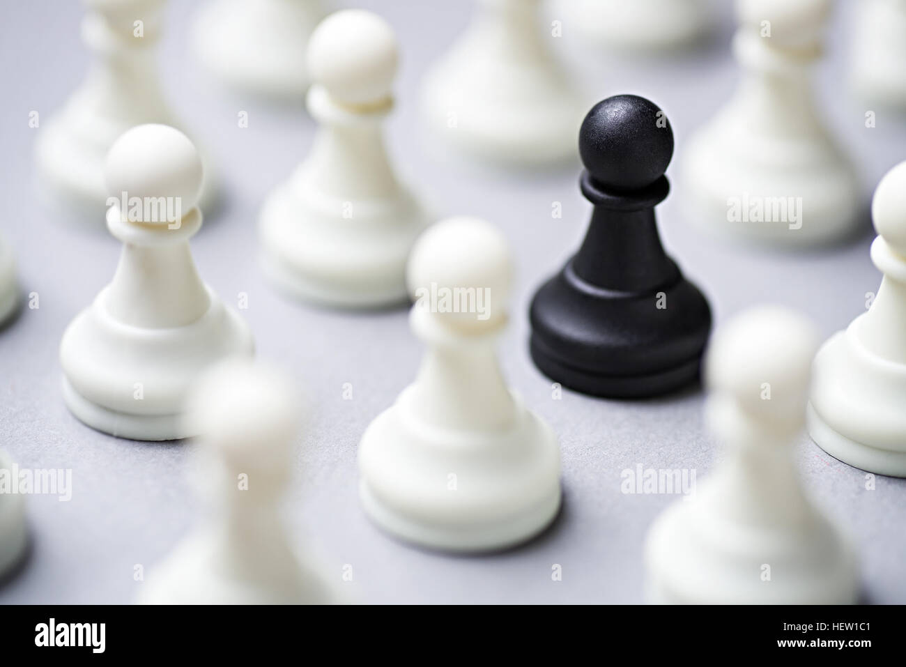Single black pawn chess piece amongst multiple white ones on a grey ...