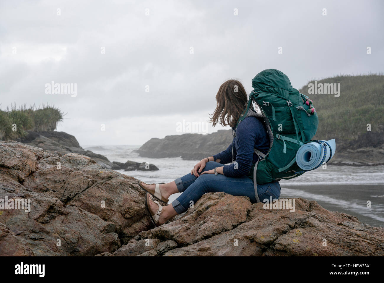 Young woman with backpack, sitting on rock, Constant Bay, Charleston ...