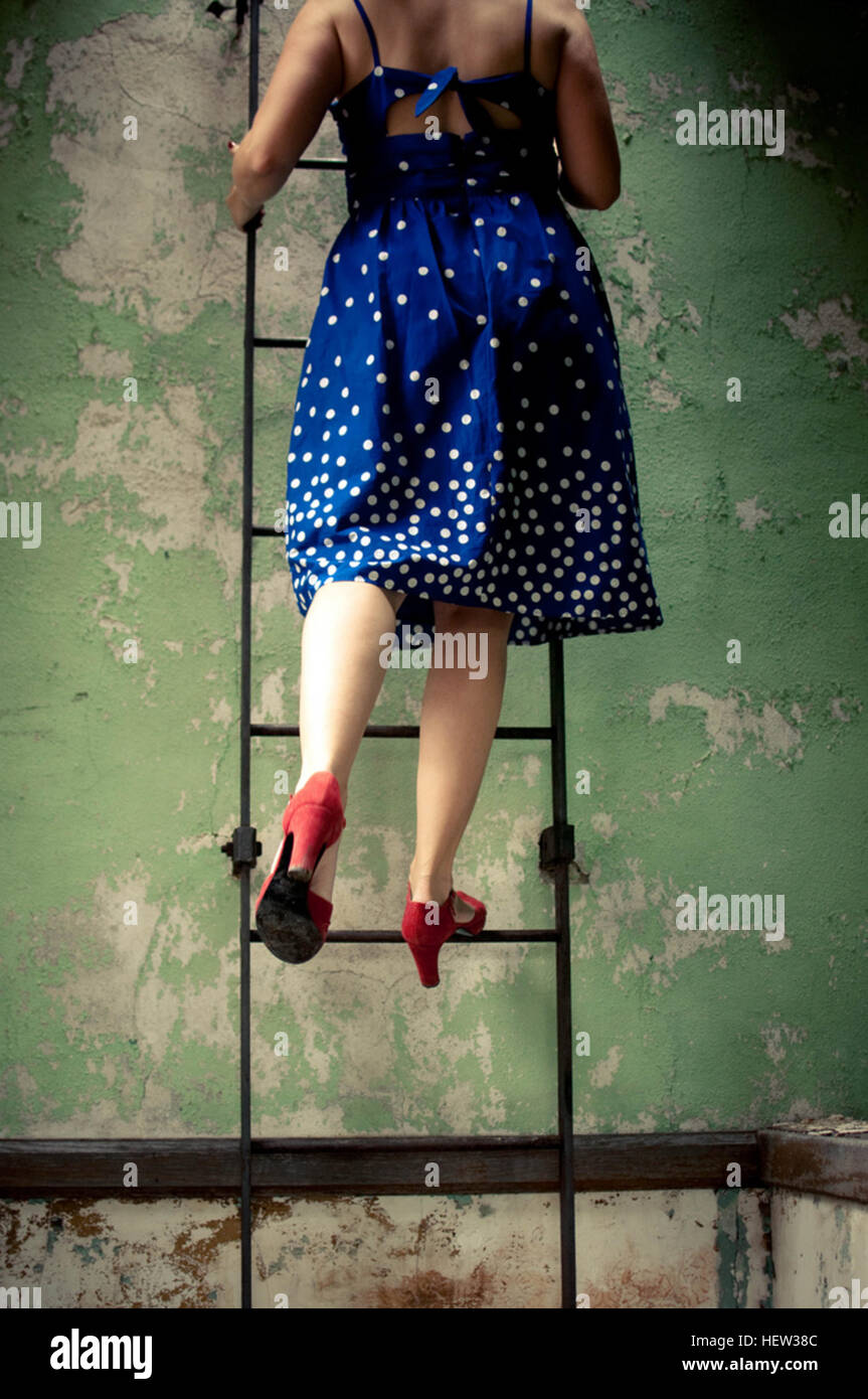 Rear view of woman wearing dress and high heels climbing ladder Stock ...