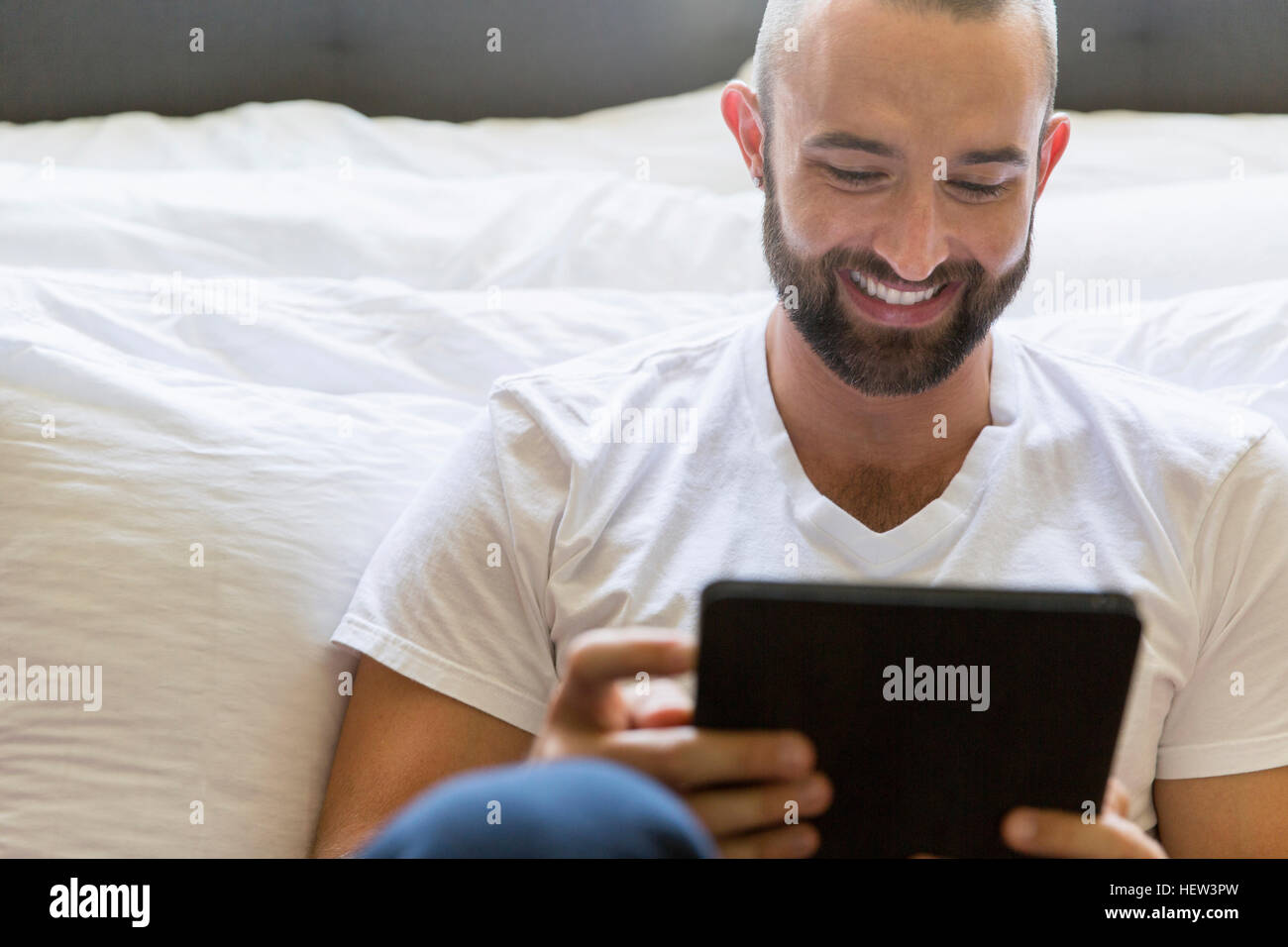 Mid adult man leaning against bed browsing digital tablet Stock Photo ...