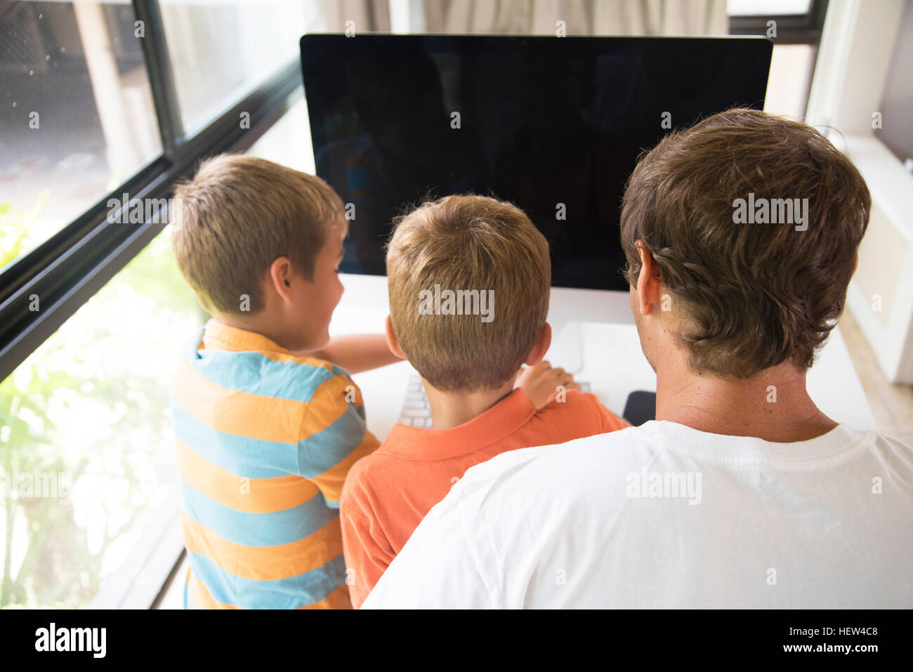 Rear view of man and two sons using desktop computer Stock Photo - Alamy